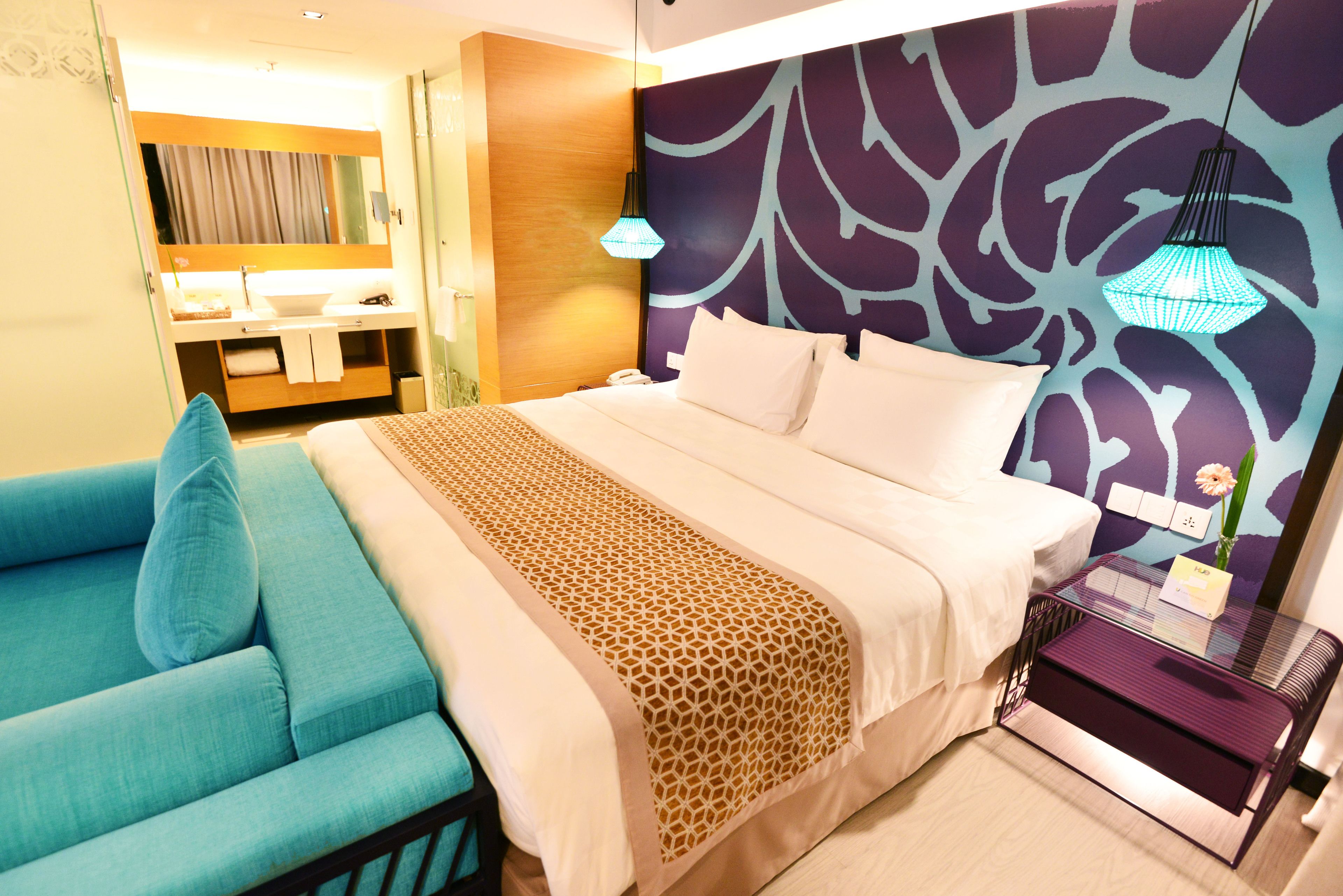 Quarto de hotel com cama, sofá, mesa de cabeceira e espelho.