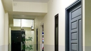 Um corredor com piso ladrilhado, um tapete verde na entrada e uma porta com janela.
