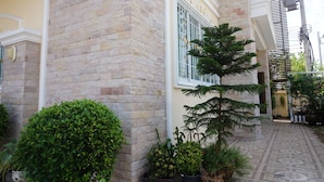 Edifício com fachada de pedra, janela com grades de metal e área de entrada com azulejos e plantas em vasos.