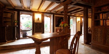 Uma área de jantar rústica com uma mesa e cadeiras de madeira, uma estante de livros e vista para o exterior.