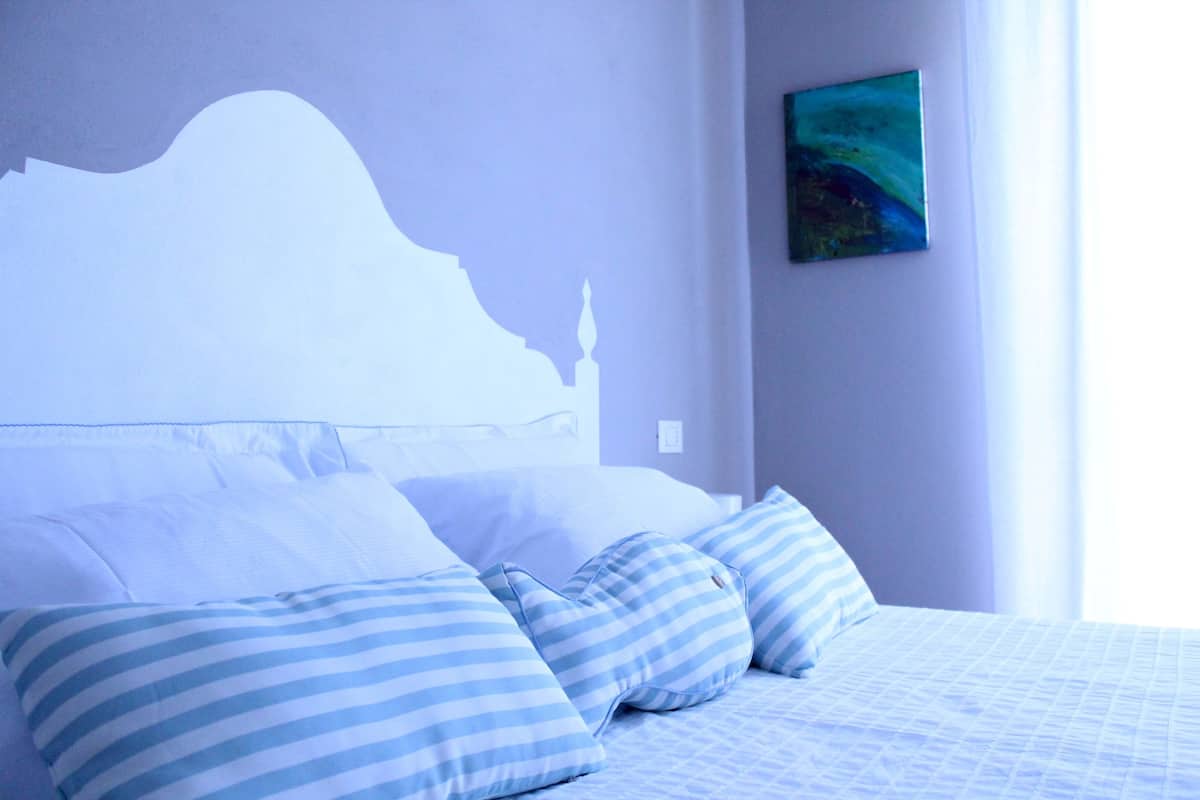 Uma cama com almofadas listradas, cabeceira e um quadro na parede.