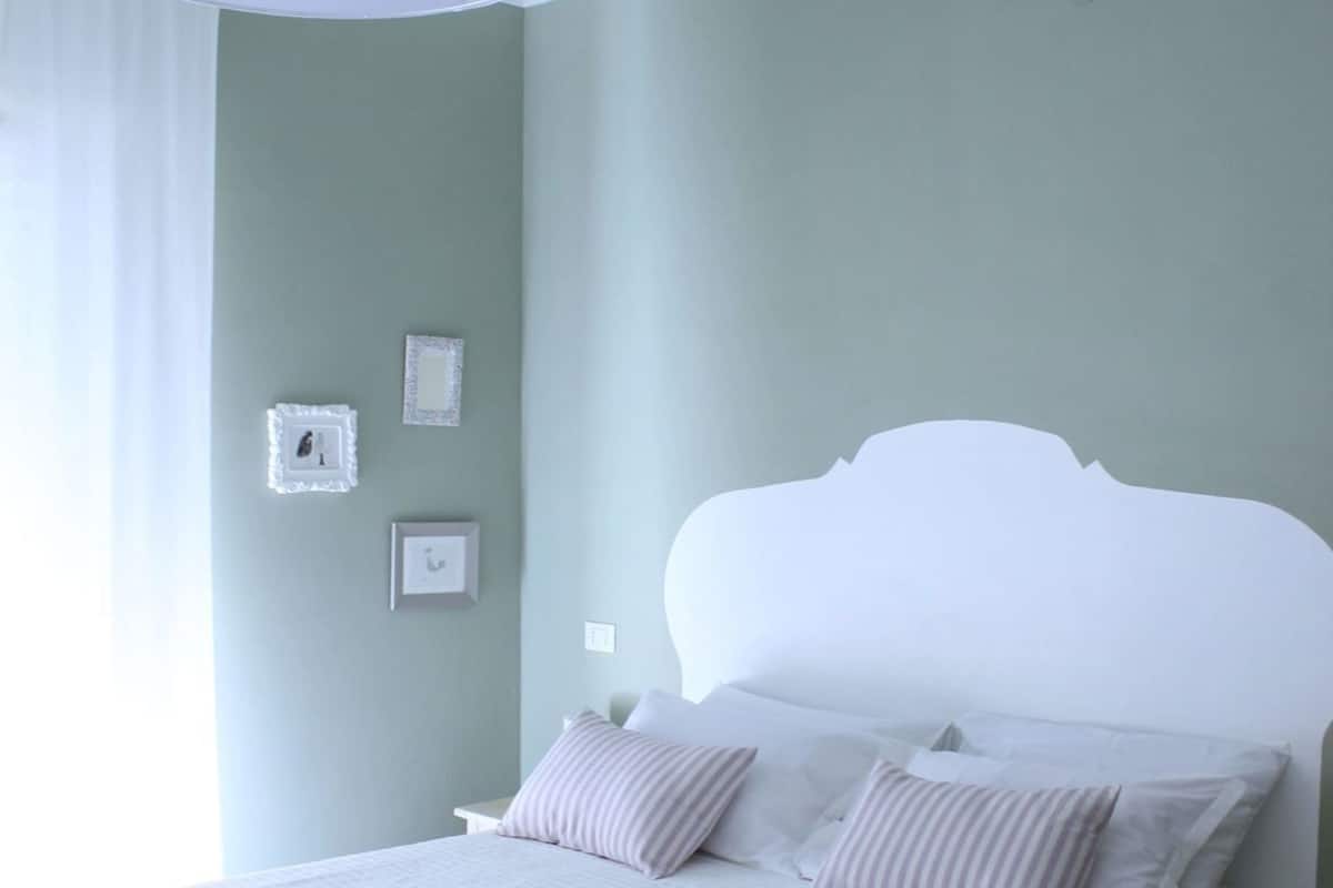 Quarto com cama, mesa de cabeceira, abajur e interruptor de luz na parede.