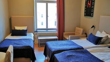 Quarto de hotel com duas camas, uma janela com cortinas, um radiador e uma cadeira.