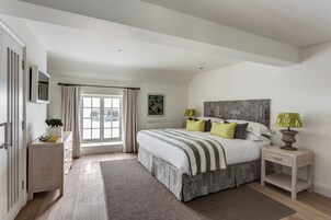 Quarto com uma cama grande, mesa de cabeceira, penteadeira, janela com cortinas e um quadro na parede.