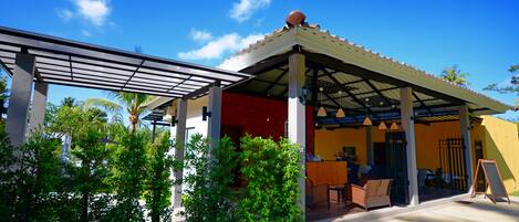 Uma área de estar ao ar livre coberta com pérgola, um balcão de recepção e vista para o verde ao redor.