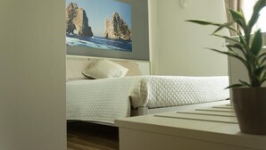 Quarto com cama, planta em vaso e pintura pendurada na parede retratando uma paisagem costeira.