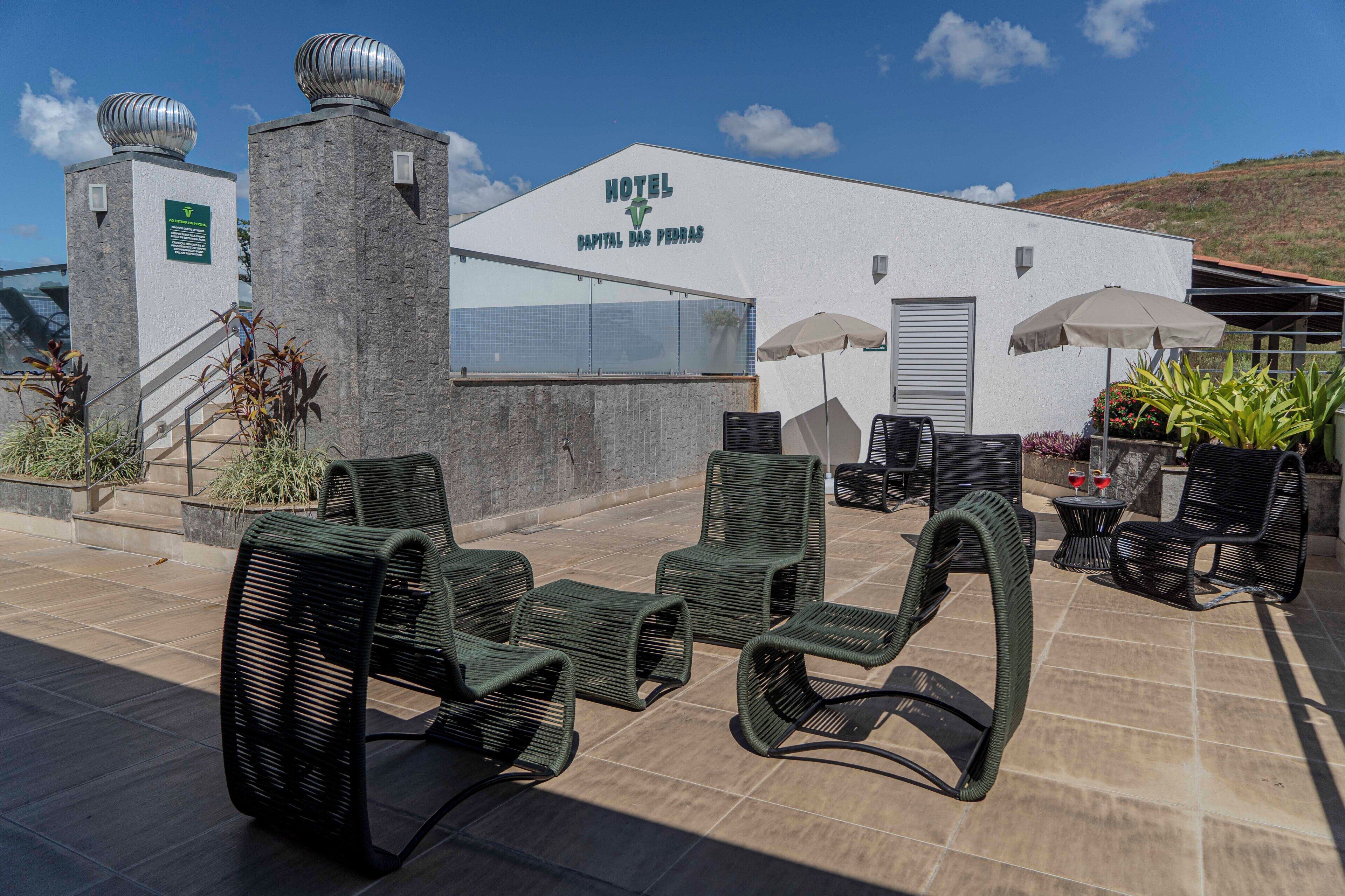 Pátio de hotel com área de estar ao ar livre, uma janela grande e uma placa com a inscrição 'HOTEL CAPITAL DAS PEDRAS'.