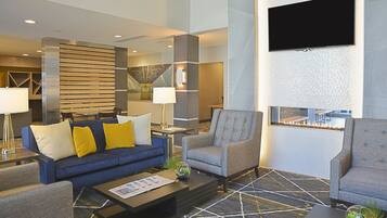 Um hall moderno com um sofá azul, poltronas, uma mesa de centro e uma televisão de tela plana na parede.