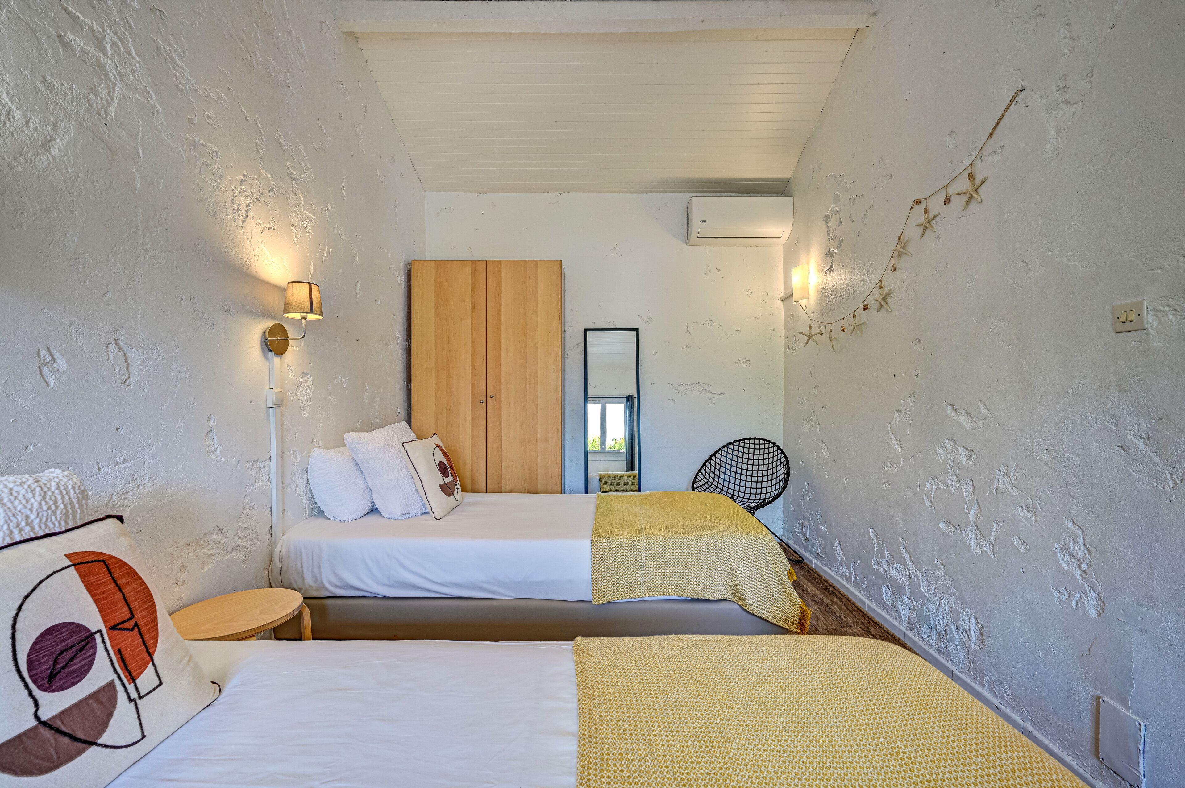 Quarto com duas camas, um guarda-roupa de madeira, um espelho e uma mesinha.