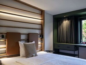 Quarto de hotel com uma cama, mesa de cabeceira, escrivaninha e janela com cortinas.
