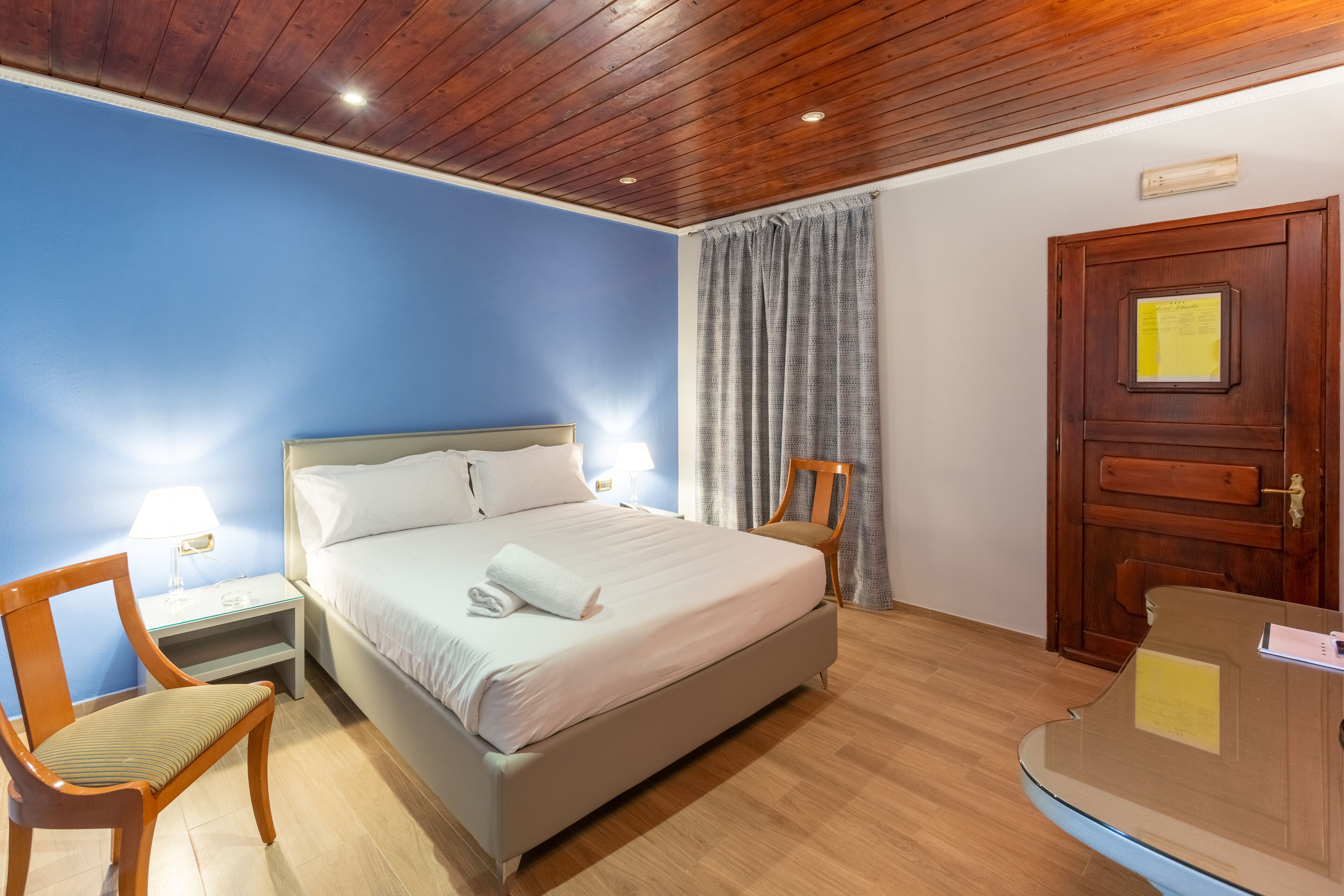 Quarto de hotel bem arrumado, com uma cama, uma cadeira, uma mesa de cabeceira e uma porta com um aviso.