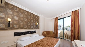 Quarto de hotel com uma cama grande, um sofá, uma escrivaninha e uma varanda com cortinas.