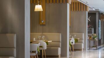 Um hall de hotel moderno com área de estar, incluindo um sofá, cadeiras, uma mesa com copos e uma luminária.