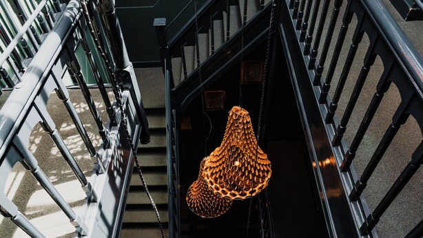 Escadaria com corrimãos de metal e duas luminárias geométricas laranja suspensas.