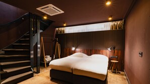 Quarto com cama, cabeceira de madeira, um pequeno banco, escada de madeira e janela com cortinas.