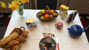 Uma mesa de café da manhã com croissants, uma cesta de frutas, um bule de chá e um jarro de leite.