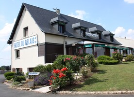 Um edifício de dois andares com uma placa que diz "HOTEL DU RELAIS". Há canteiros de flores com flores vermelhas e roxas em frente ao edifício.