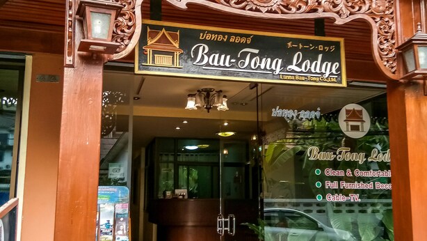 A entrada da Pousada Bau-Tong, com uma placa, esculturas em madeira e uma porta de vidro.