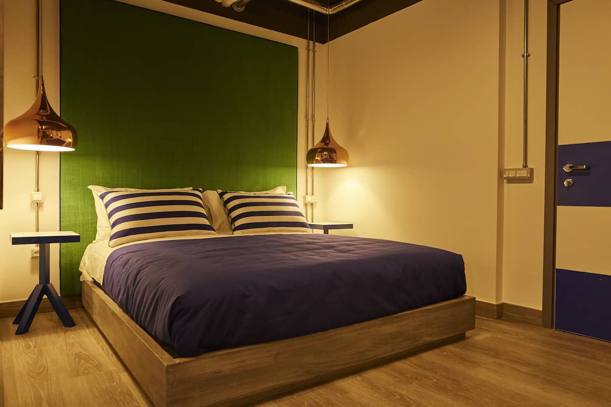 Quarto com cama, duas mesas de cabeceira, uma parede verde e uma porta.