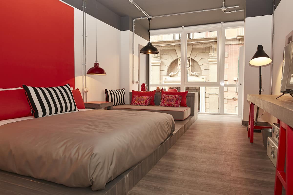 Quarto moderno com cama grande, parede de destaque vermelha e vista pela ampla janela.
