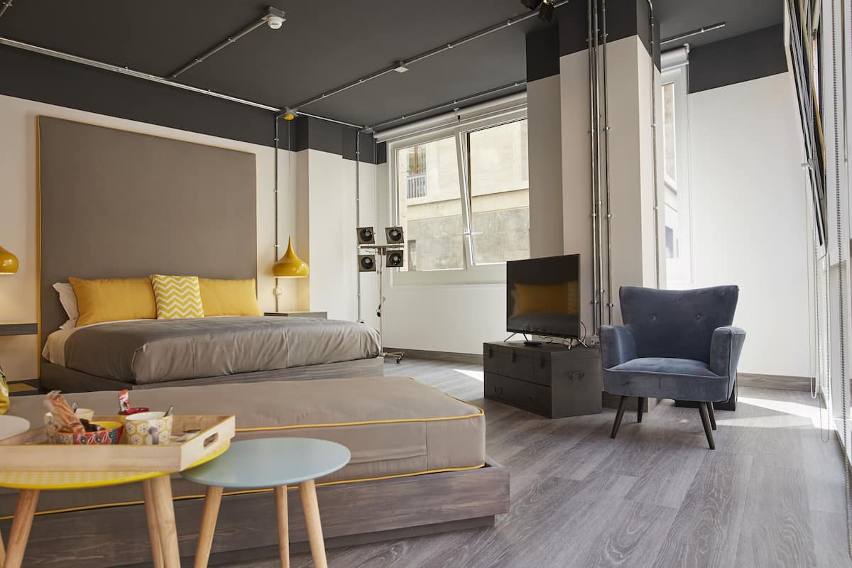Quarto moderno com cama, mesa de cabeceira, televisão e uma cadeira.