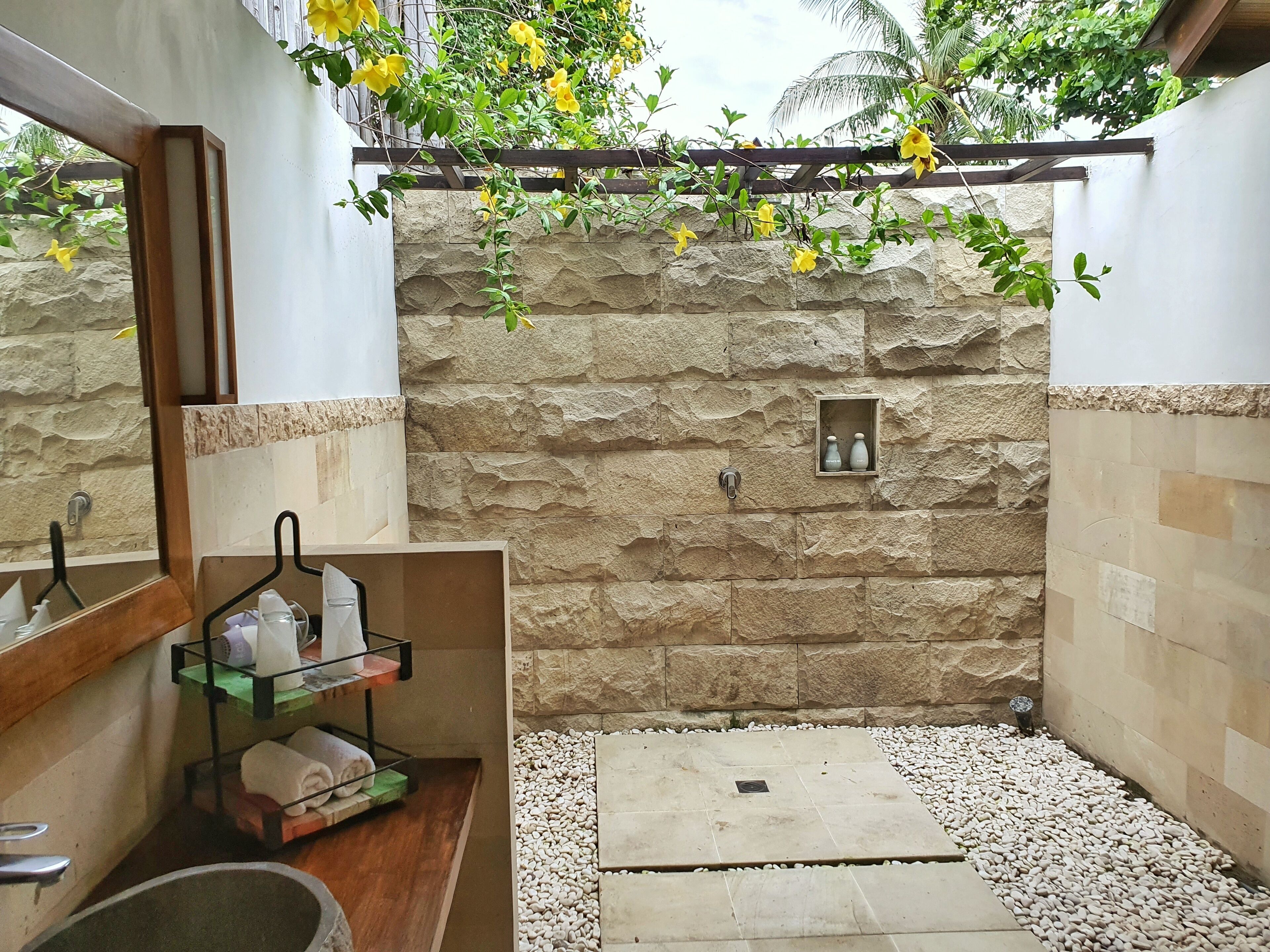 Uma casa de banho com parede de pedra, um banco de madeira, um espelho e uma pequena prateleira com toalhas e produtos de higiene pessoal.