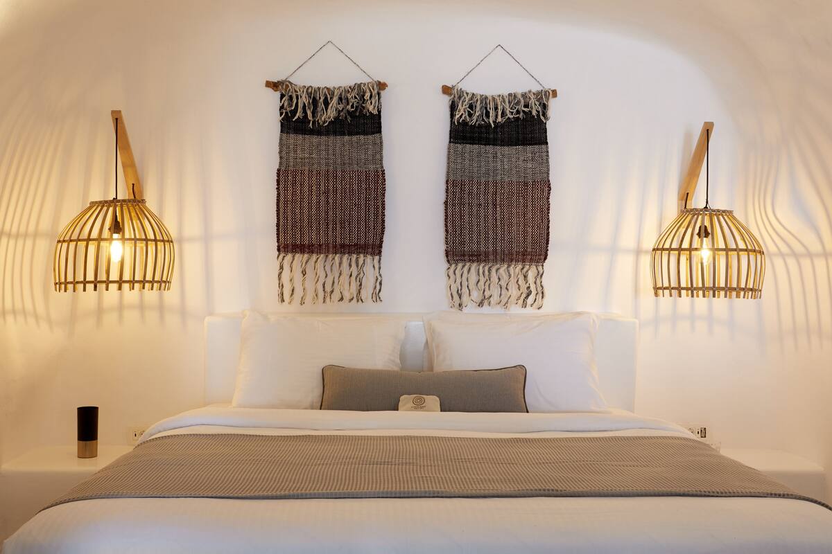 Cama bem arrumada com cabeceira, duas luminárias na parede e uma mesinha de cabeceira com abajur.