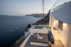 Uma varanda com vista para o mar, uma banheira de hidromassagem e um espaço de estar com almofadas e uma toalha.