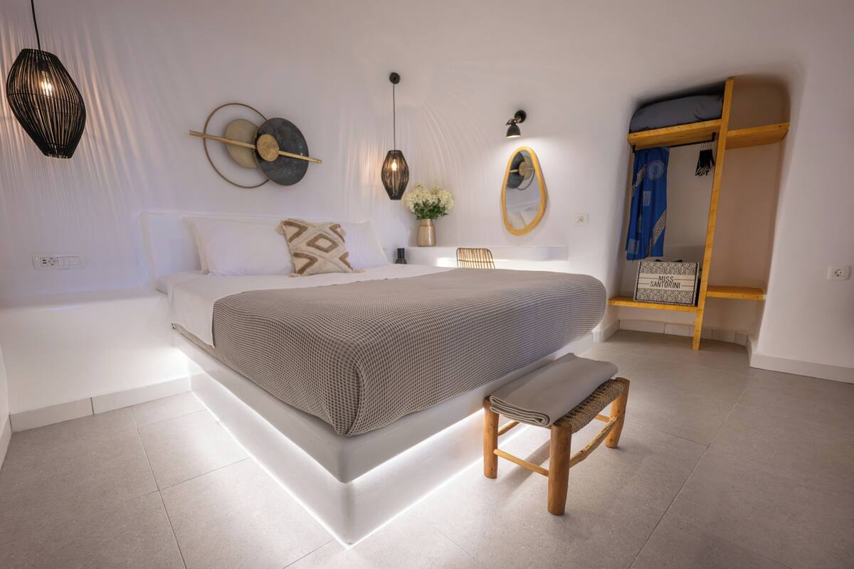Quarto moderno com cama, mesa de cabeceira, abajur, espelho e um banco embutido.