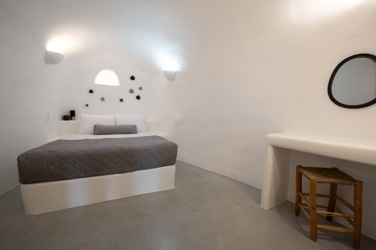 Quarto moderno com cama, mesa de cabeceira e um banquinho.