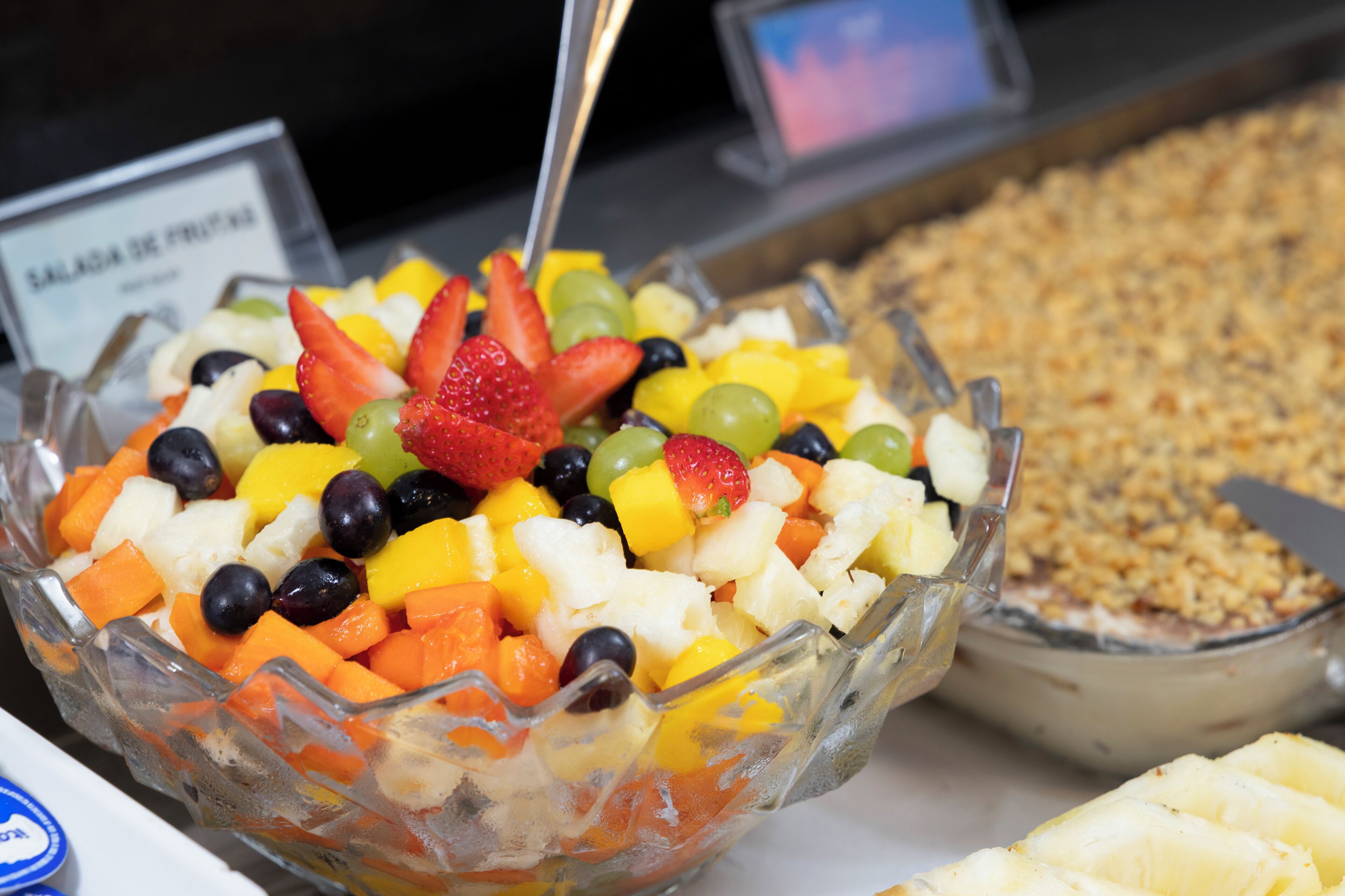 Uma tigela de salada de frutas com diversas frutas e uma colher.