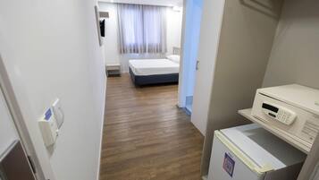 Quarto de hotel com cama, mesa de cabeceira pequena, micro-ondas e geladeira.