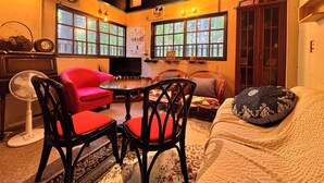 Um quarto acolhedor com um sofá vermelho, duas cadeiras pretas, uma mesa redonda pequena e uma cama com almofada estampada.