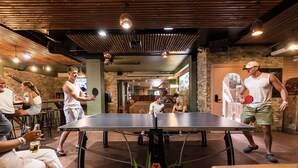 Ambiente interno informal com mesa de pingue-pongue, paredes de tijolo e teto de madeira.
