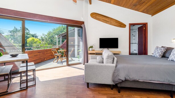 Quarto moderno com cama grande, TV de tela plana e varanda com área de refeições.