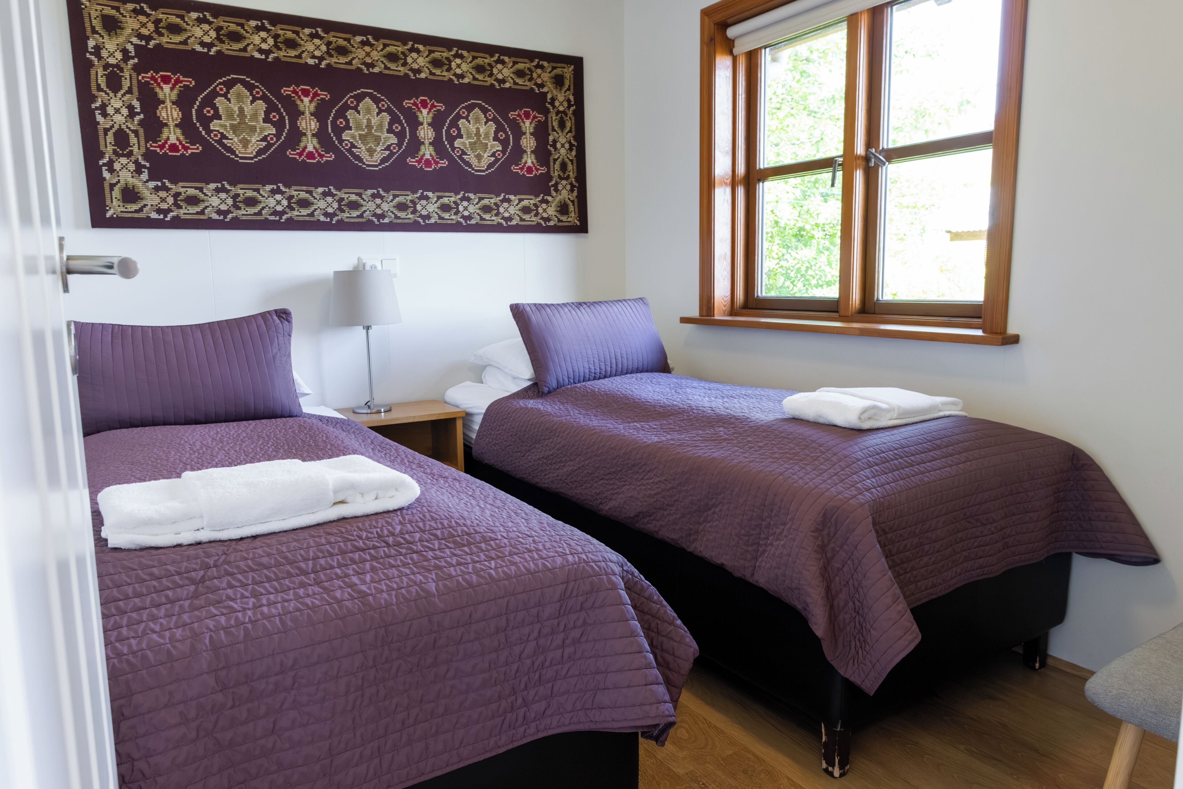 Quarto com duas camas, uma janela, mesa de cabeceira e luminária na parede.