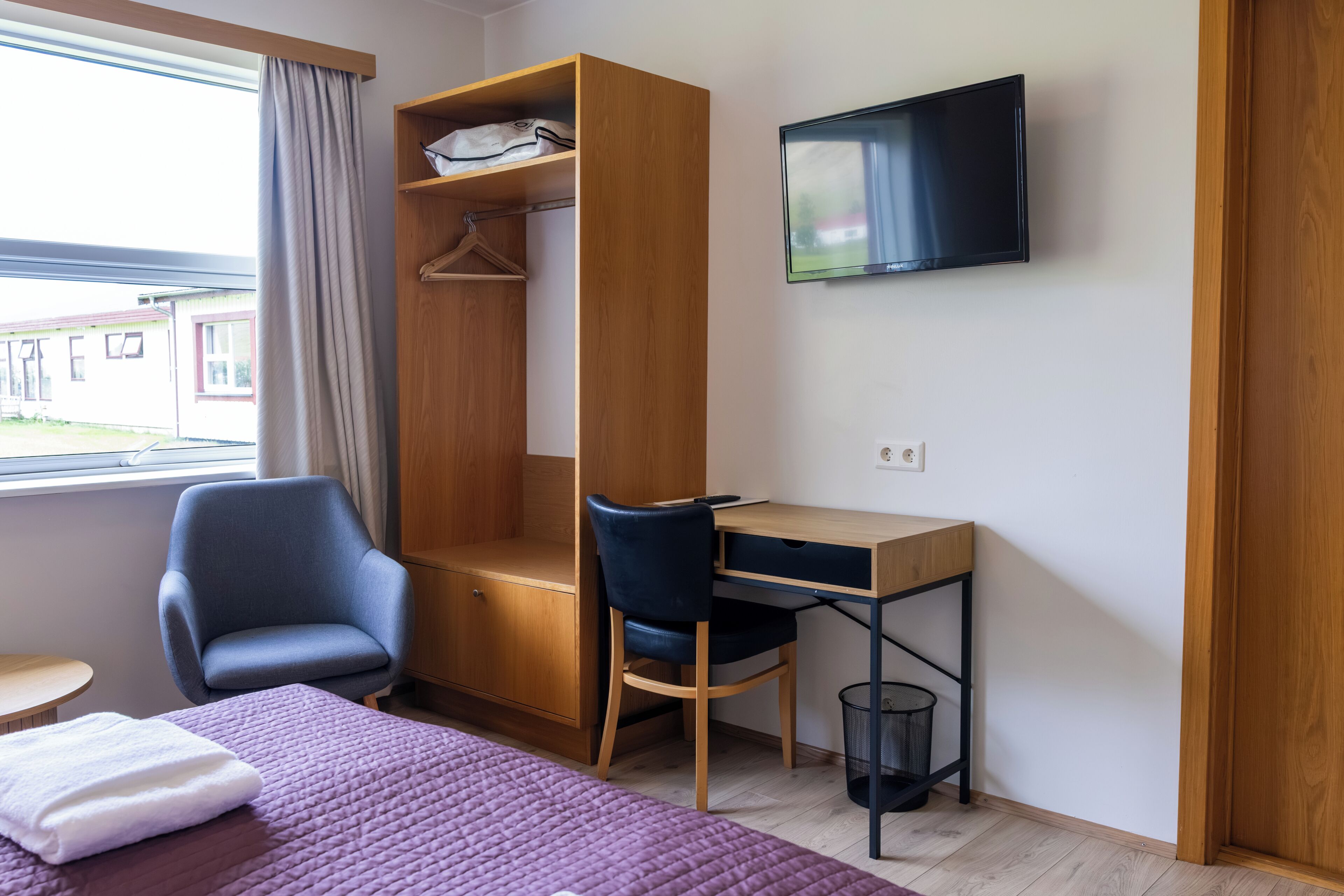 Quarto com cama, escrivaninha, cadeira, televisão e guarda-roupa.