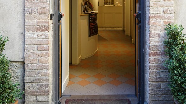 Entrada do Piccolo Hotel, com um arco de pedra e piso de azulejos.
