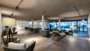 Amplo espaço interno com móveis de vime, janelas grandes e vista para a cidade.