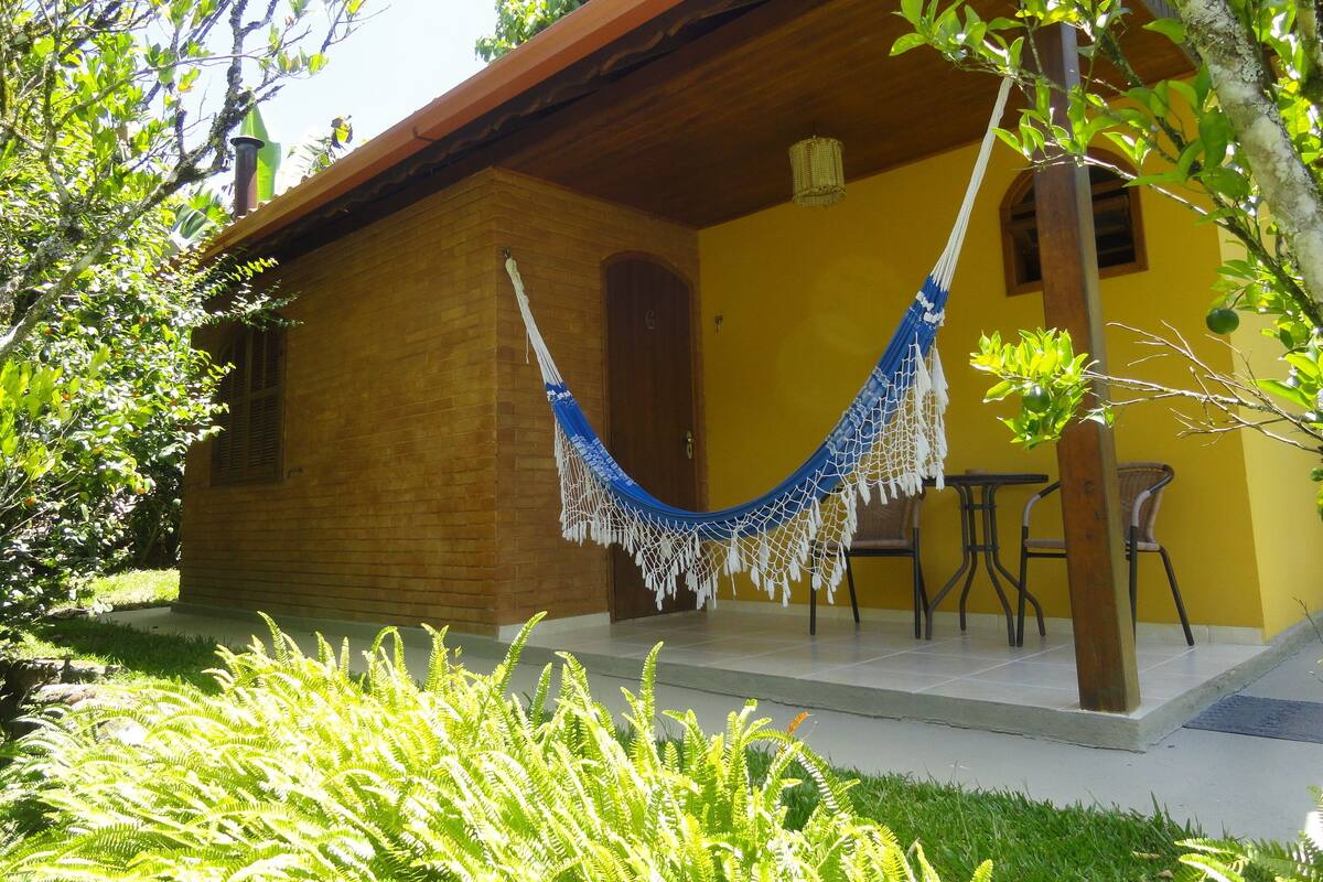Um edifício amarelo com uma rede pendurada em uma árvore, um pátio com cadeiras e um muro de tijolos.