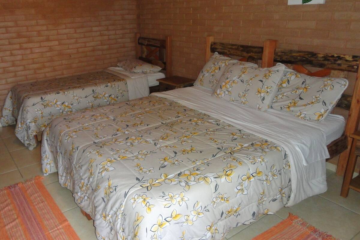 Quarto com duas camas, cada uma com roupa de cama florida, parede de tijolos e chão ladrilhado.