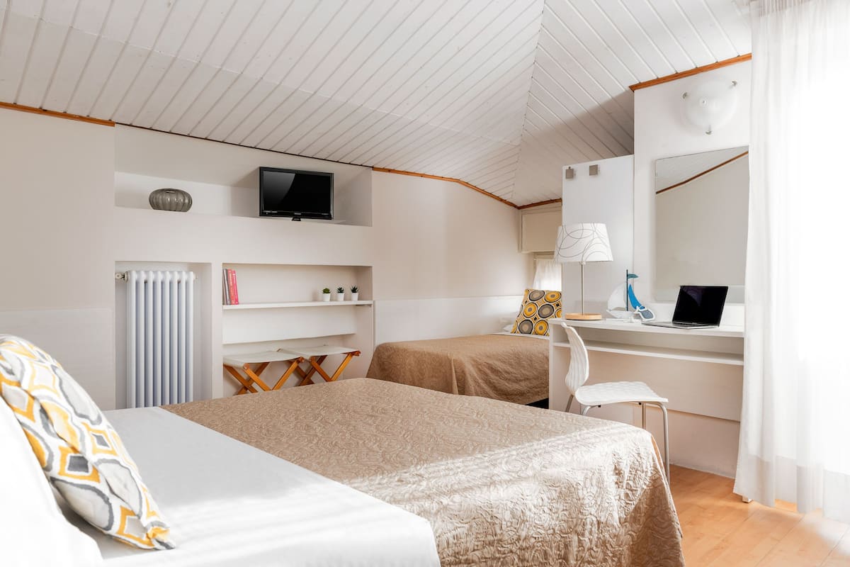 Quarto com duas camas, uma escrivaninha com um laptop, uma televisão e um espelho.
