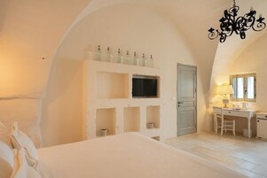 Quarto com cama, escrivaninha, cadeira, televisão e lustre.