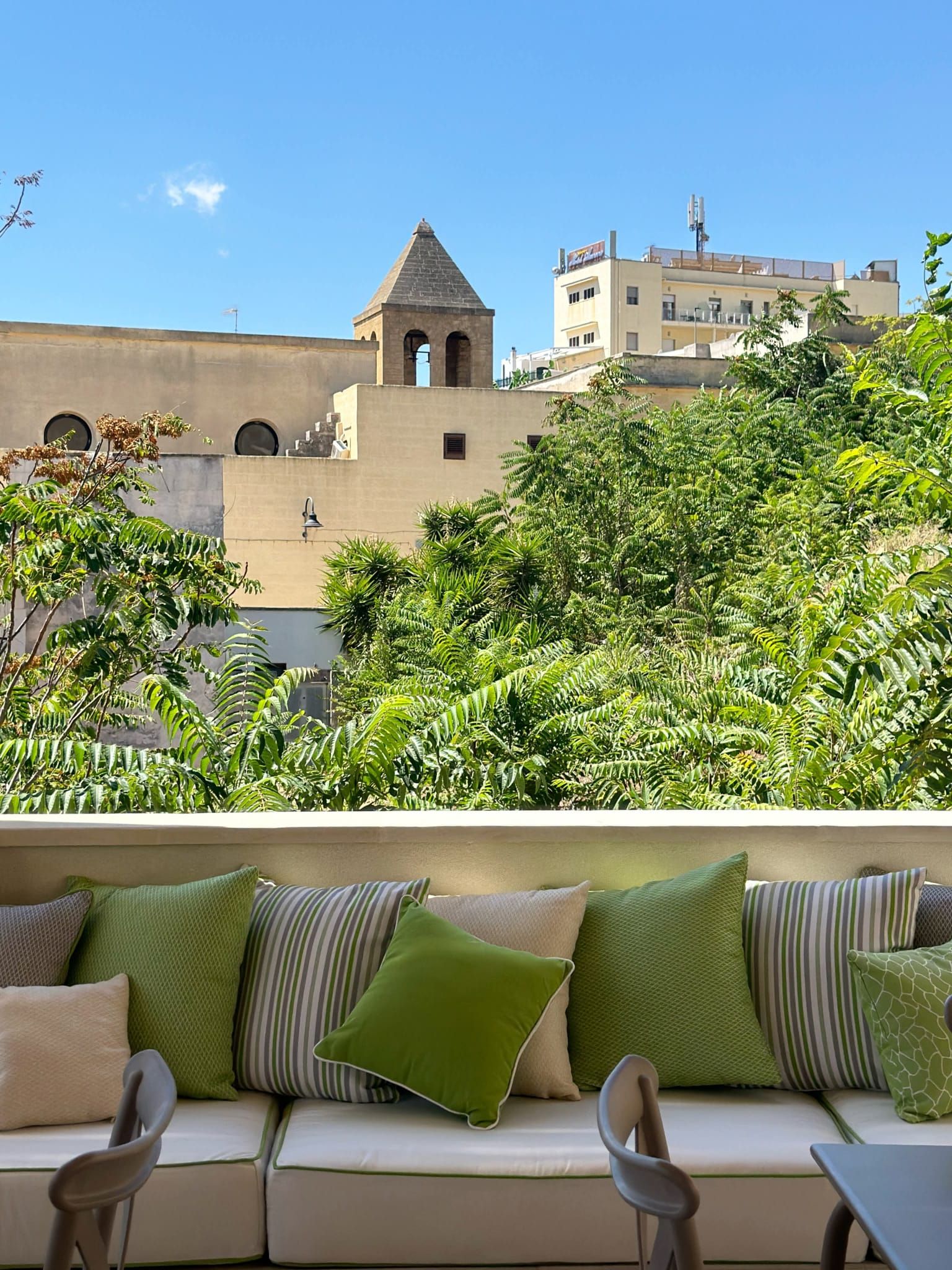 Terraço no telhado com área de estar, vegetação exuberante e vista para um edifício com torre.