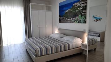 Quarto com cama, mesa de cabeceira, guarda-roupa e pintura de uma paisagem costeira.