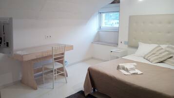 Quarto com cama, escrivaninha, cadeira, janela e radiador.