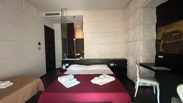 Quarto de hotel com cama grande, escrivaninha, cadeira e um banquinho.