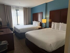 Quarto de hotel com duas camas, uma escrivaninha, uma cadeira e janela com cortinas.