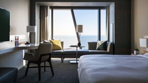 Quarto de hotel com uma cama grande, uma escrivaninha, uma cadeira e vista para o oceano.