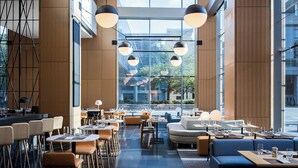 Restaurante moderno com pé-direito alto, grandes janelas e diversos tipos de assentos, incluindo mesas e sofás.